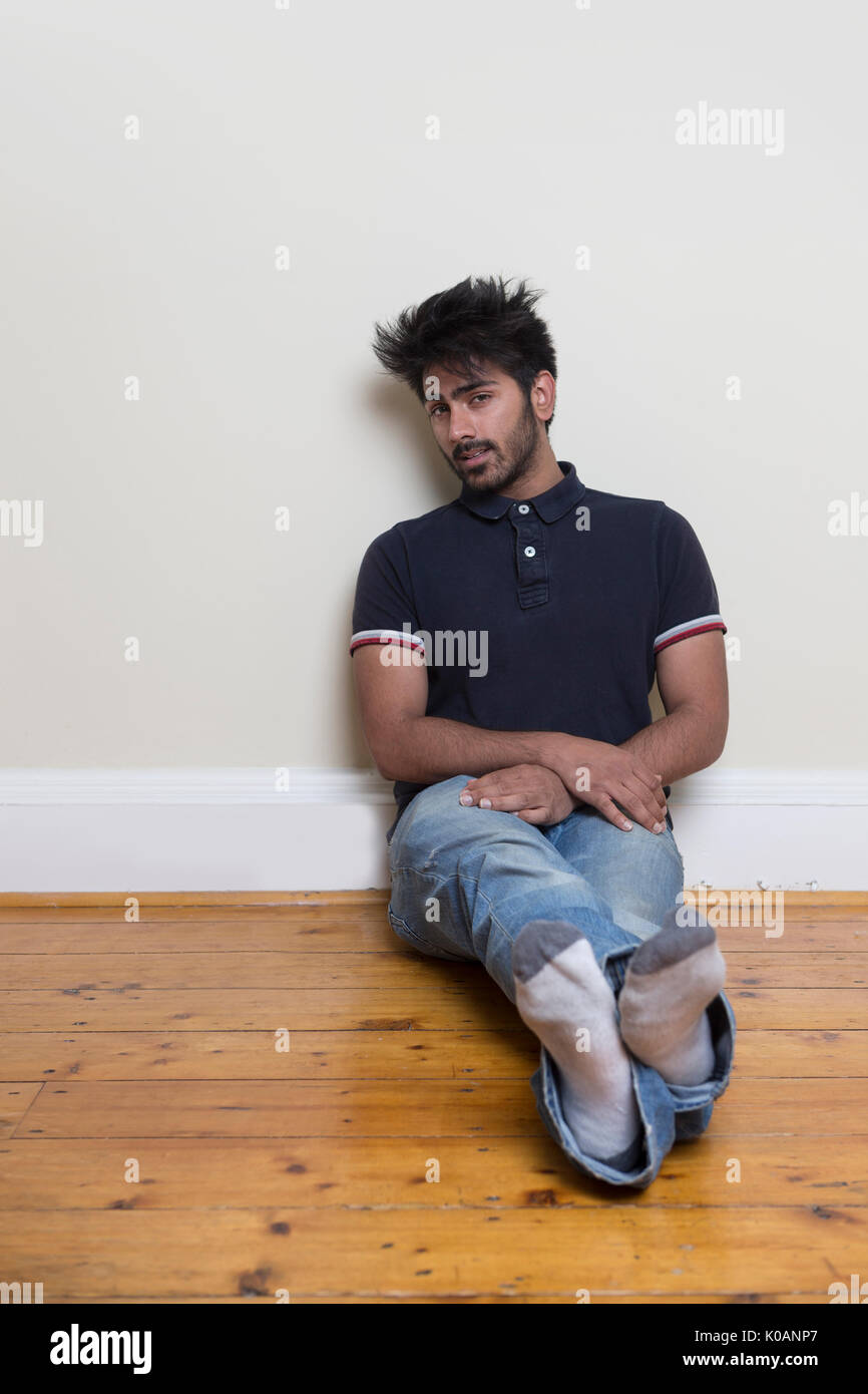 Portrait of a happy Indian man sitting on floor against green wall ...
