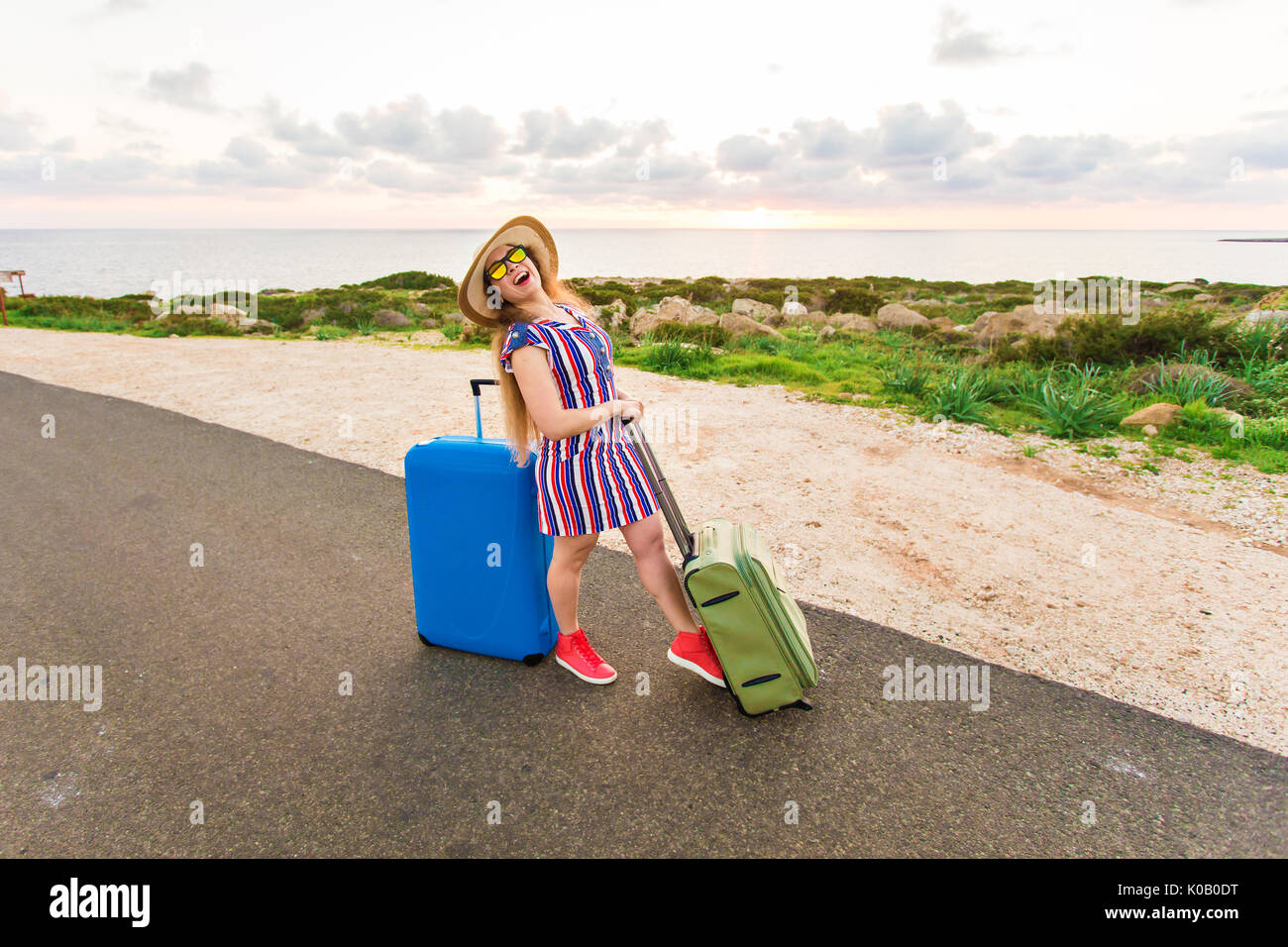 Happy cheerful traveler woman standing with suitcases on the road and ...