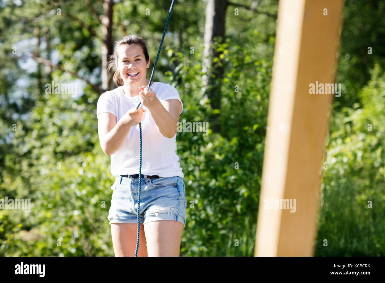 Woman Smiling While Pulling Rope Attached To Wooden Structure Stock ...