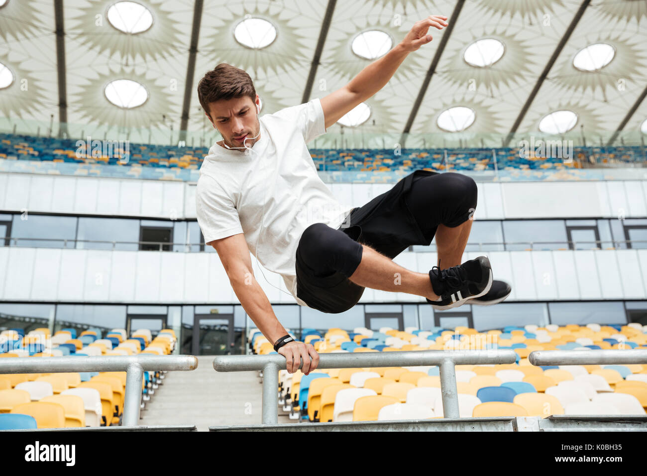 Image of young sports man jumping at the stadium outdoors listening ...