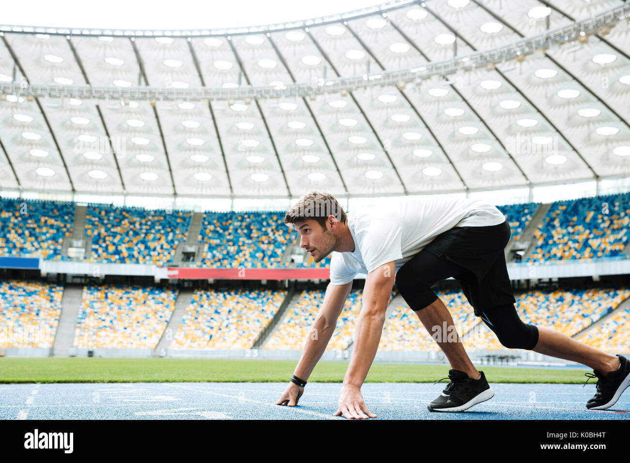 Side view of a young athlete at starting position ready to start a race ...