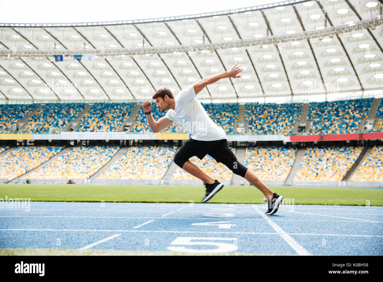 Side view of a sport man running on a racetrack at the stadium Stock ...