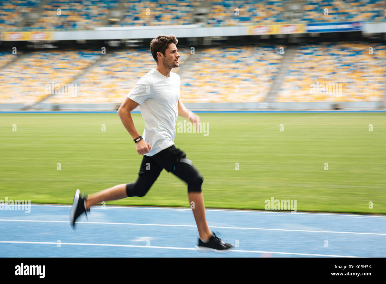 Side view of a young sportsman running on a racetrack at the stadium ...