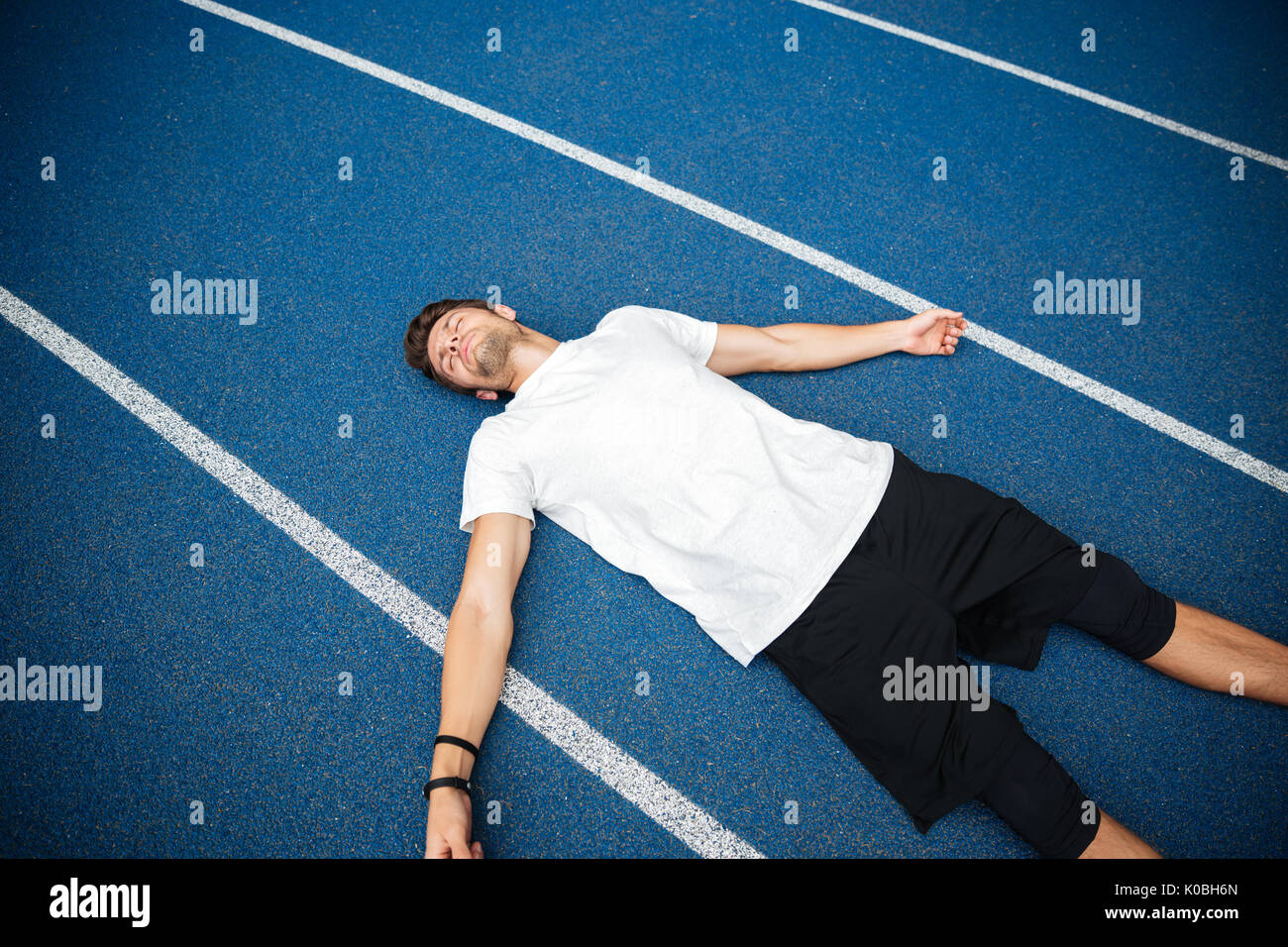 Tired male athlete resting after running while lying on a racetrack at ...