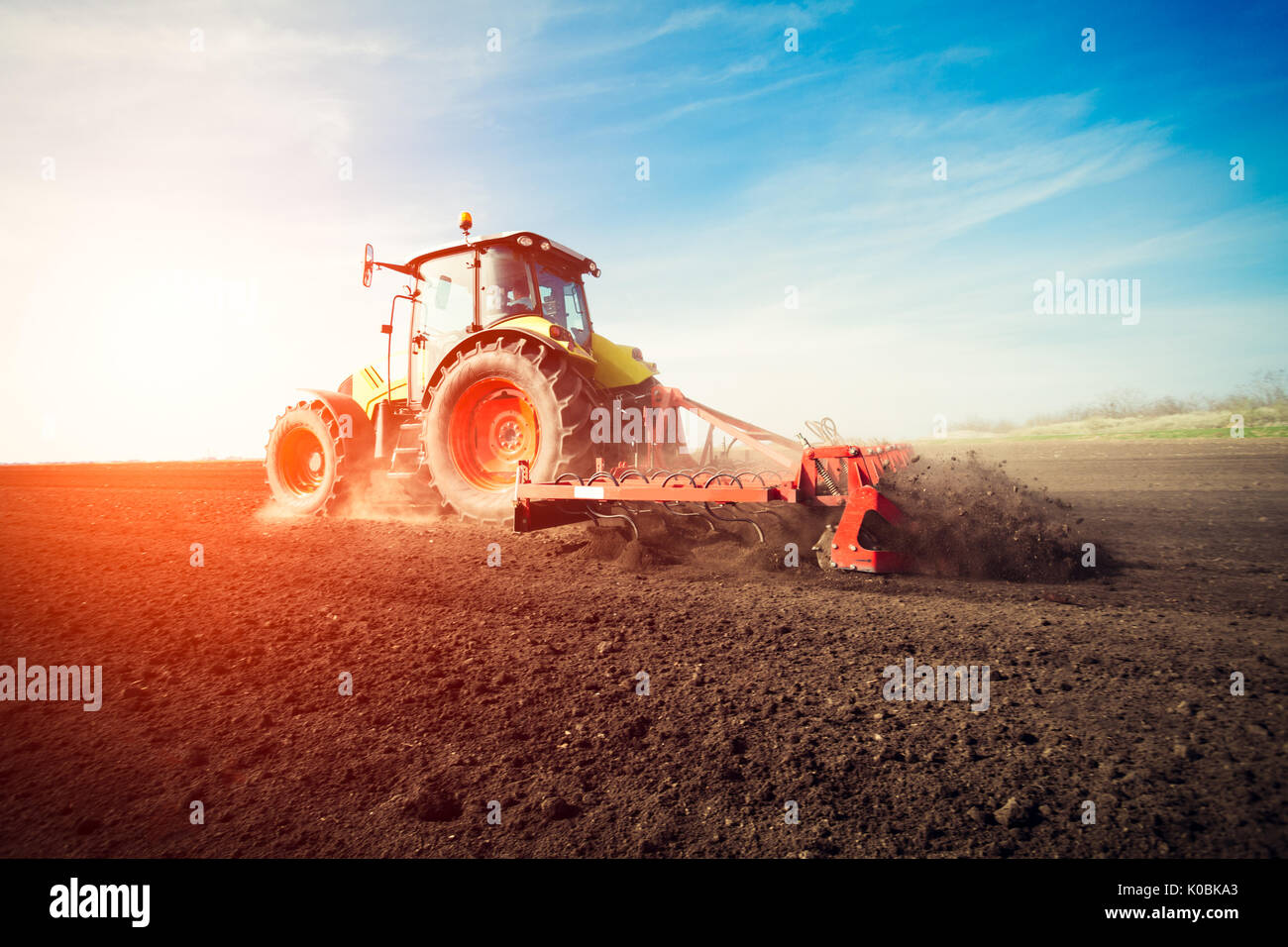 Tractor working on farm land on sunset Stock Photo - Alamy