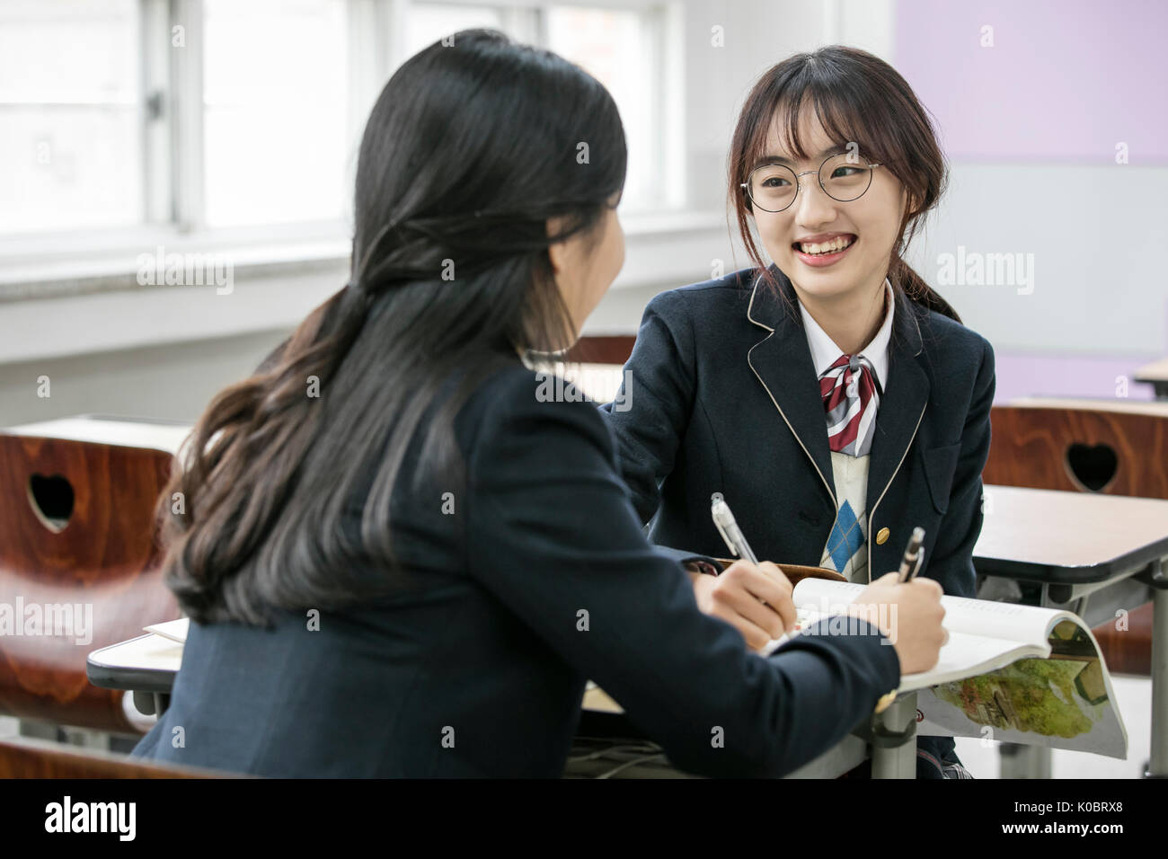 Portrait of two smiling school girls sitting in classroom Stock Photo ...