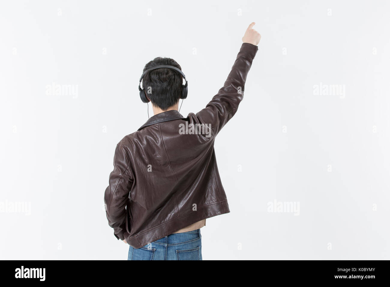 Back of young man in leather jacket listening to music pointing up ...