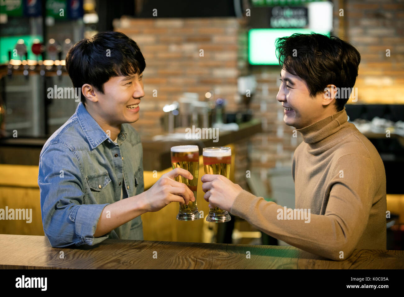Portrait of two smiling men toasting with beer face to face at bar ...