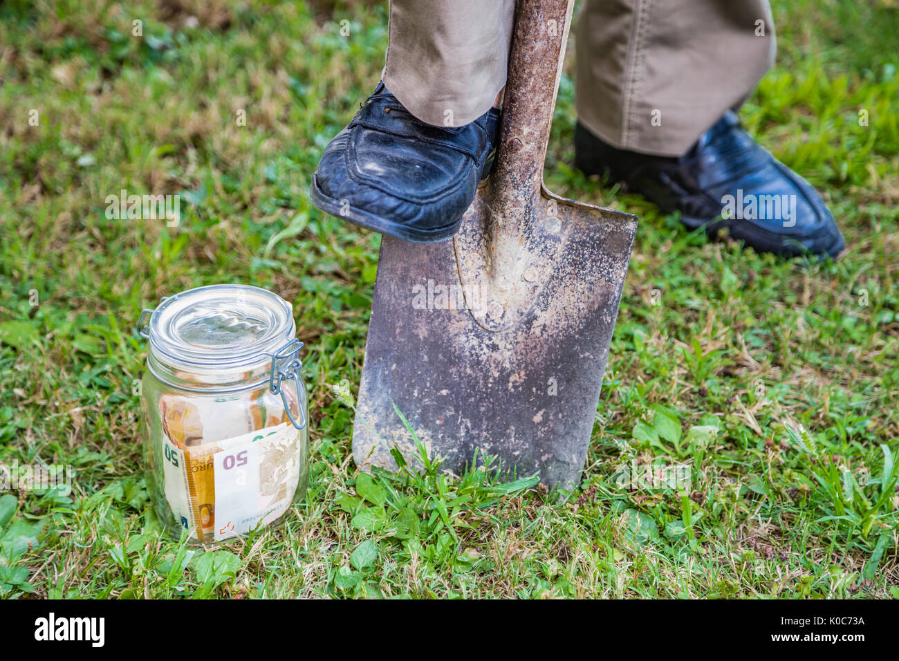 Burying a jar of money into the ground by digging a hole with a shovel ...