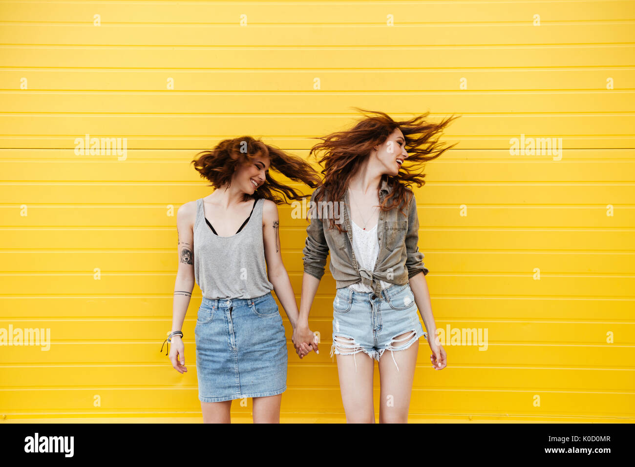 Picture of two young smiling women friends standing over yellow wall ...