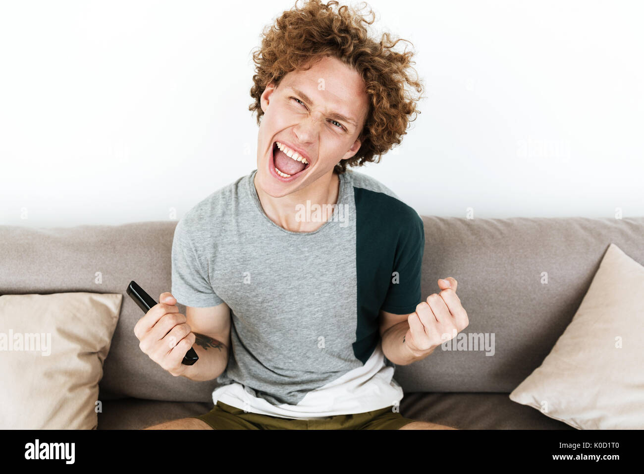Image of handsome happy man sitting on sofa holding remote control make ...