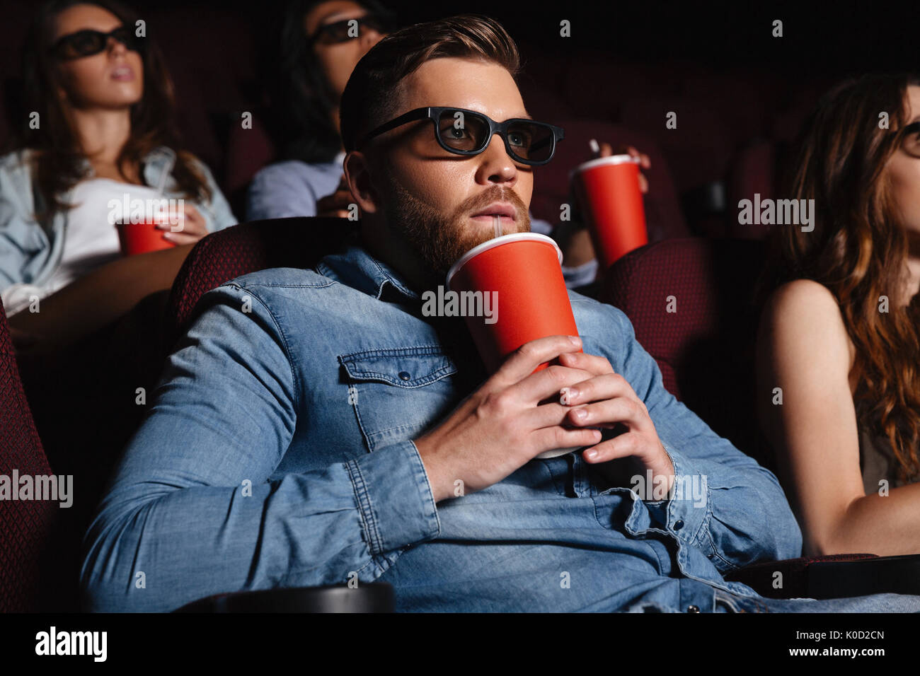 Photo of concentrated young man sitting in cinema watch film drinking ...