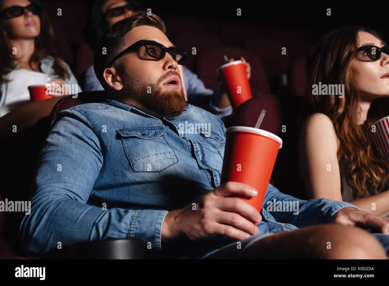 Image of shocked young man sitting in cinema watch film drinking ...
