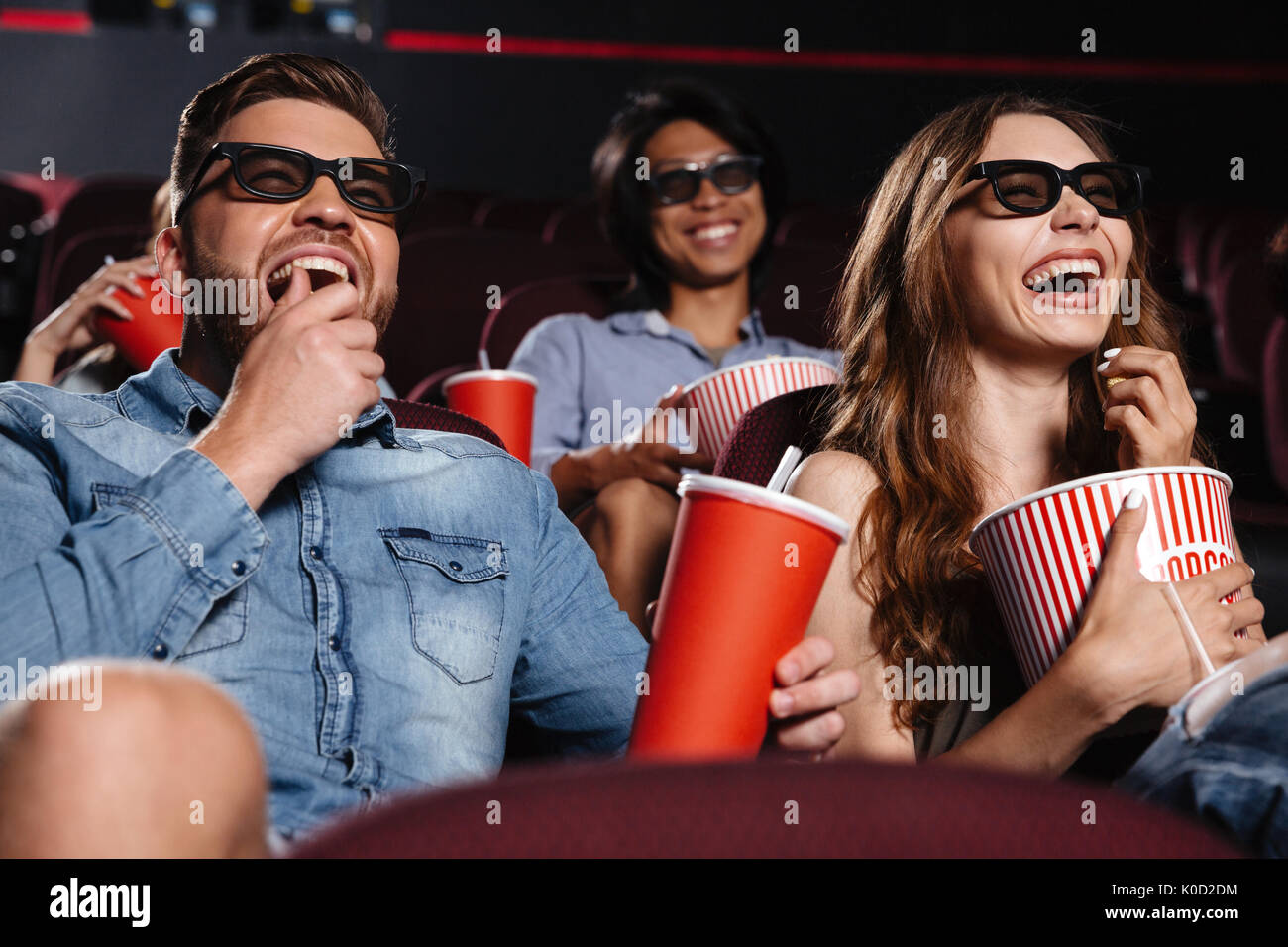 Image of laughing friends sitting in cinema watch film eating popcorn ...
