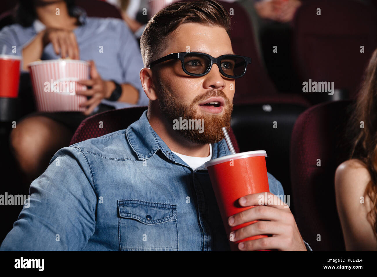 Photo of concentrated young man sitting in cinema watch film drinking ...