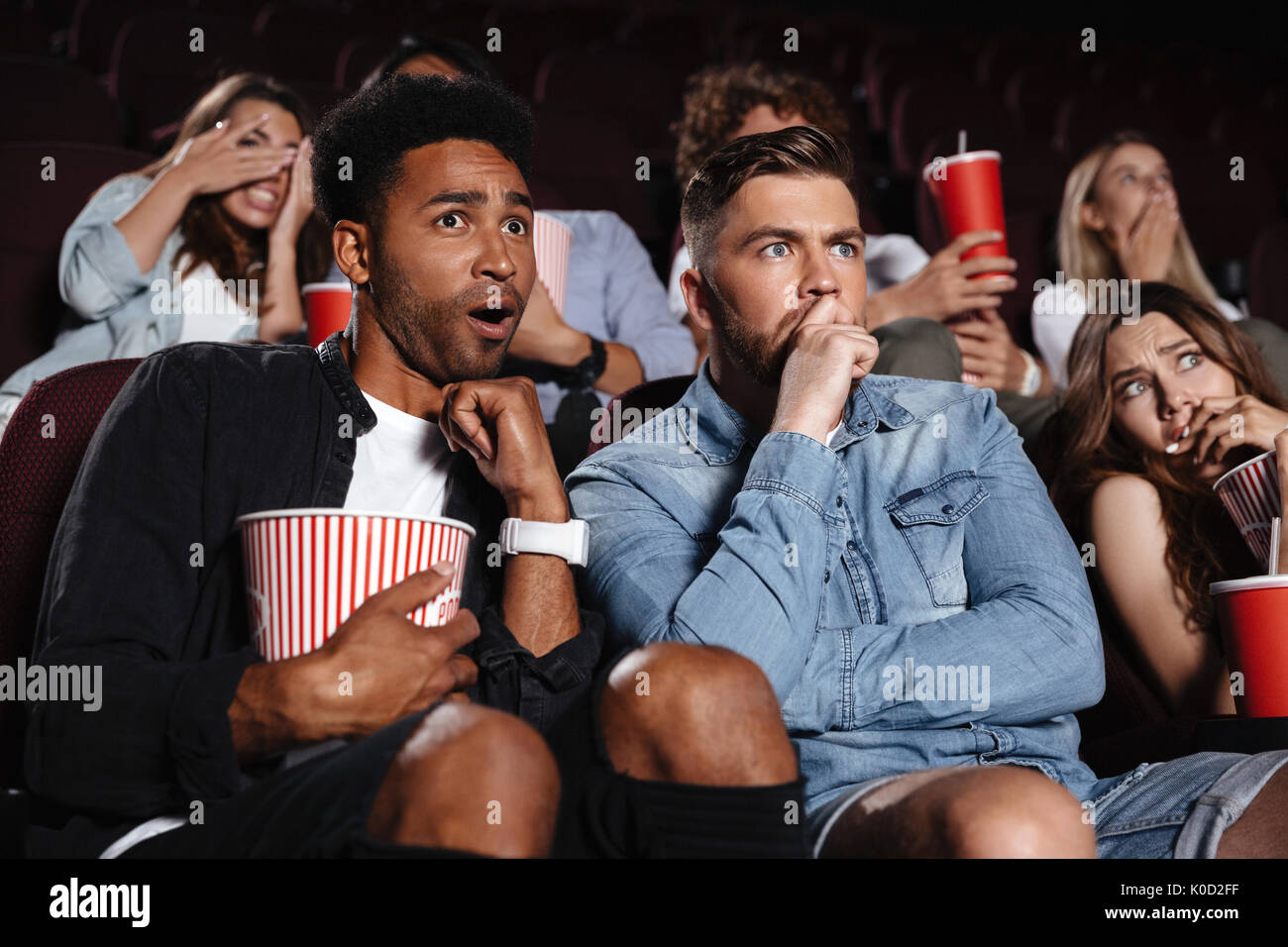 Image of shocked scared young friends sitting in cinema watch film ...