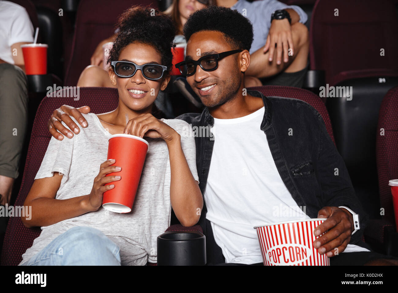 Happy afro american couple watching 3D movie and eating popcorn while sitting in a movie theater ...