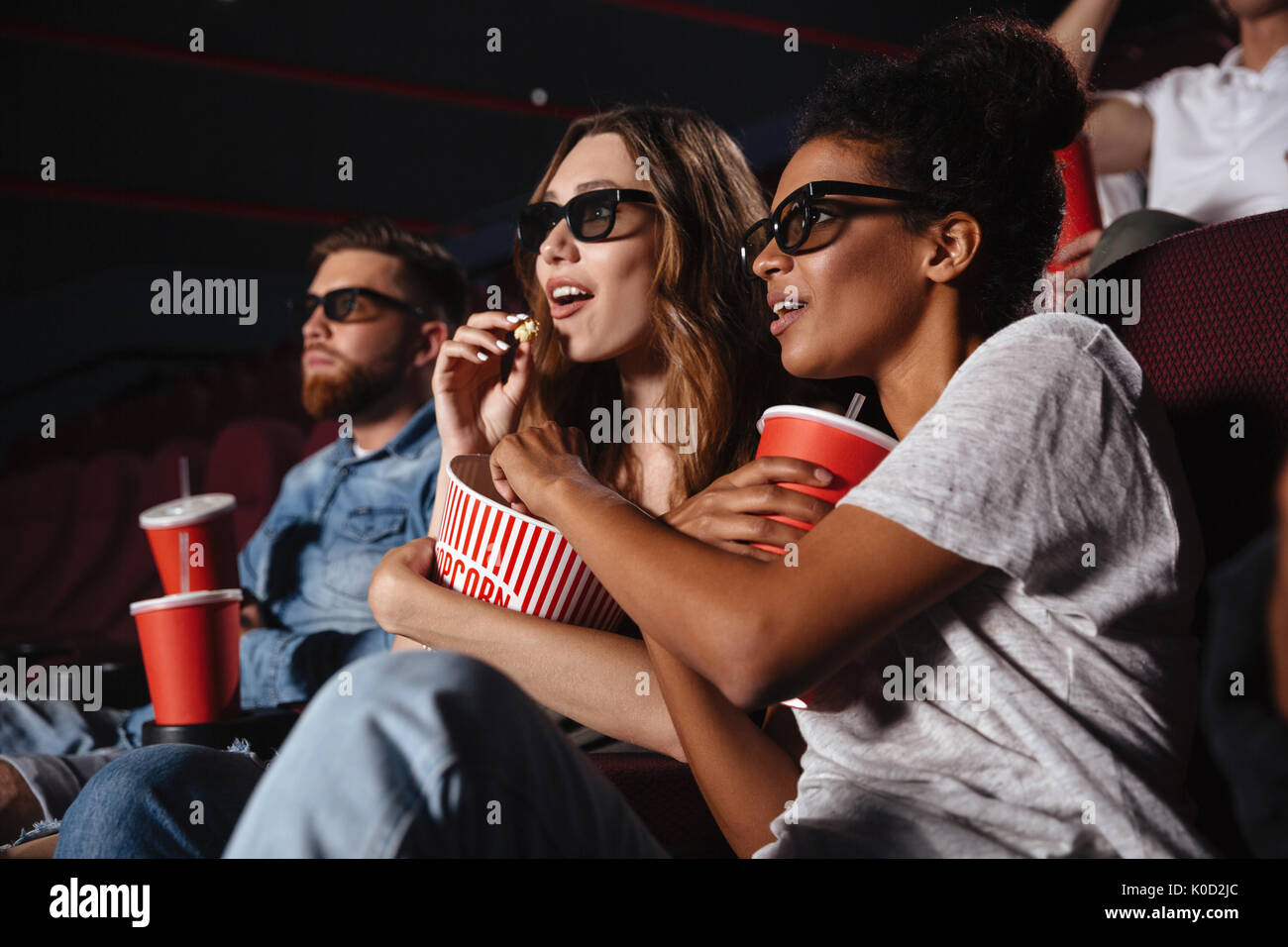 Two young women in eyeglasses watching 3d movie and eating popcorn ...