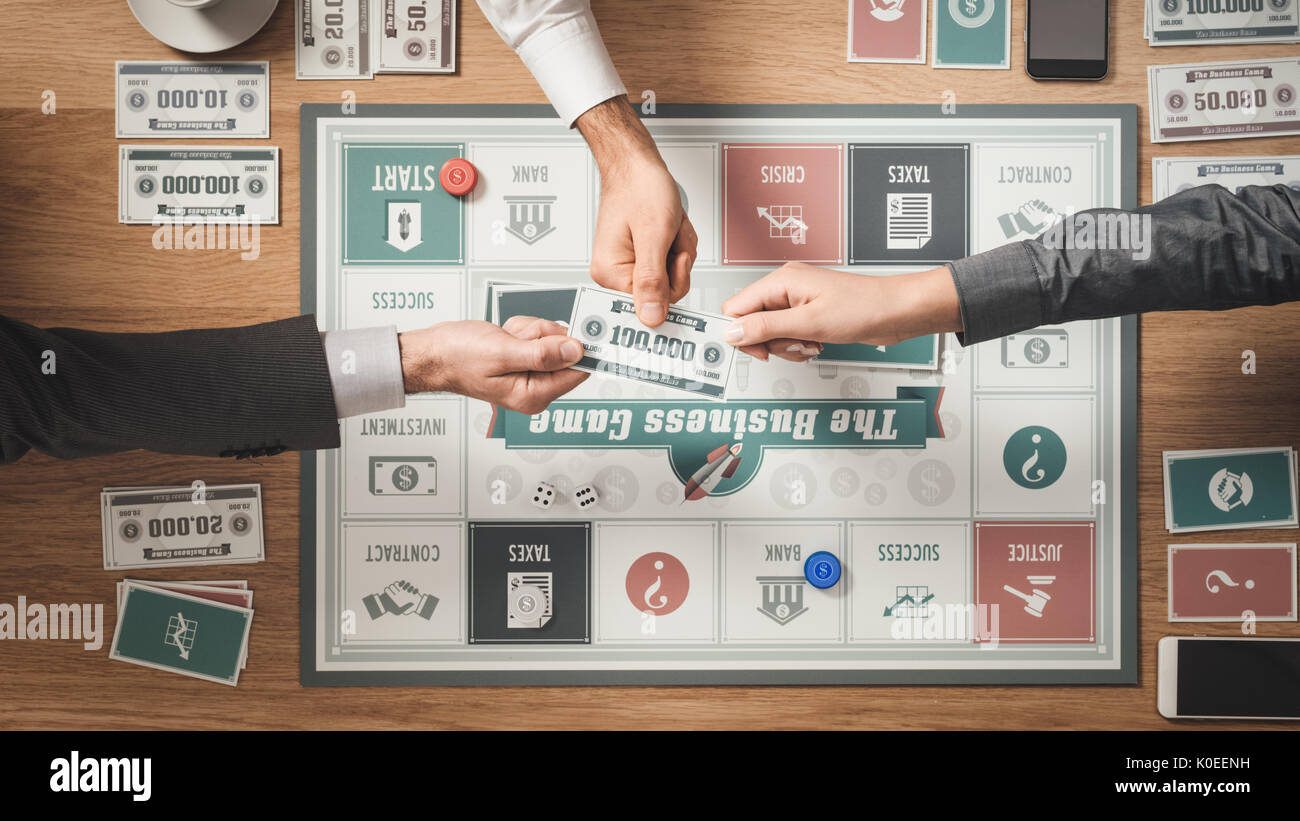 People playing a business board game on a wooden table challenging each ...