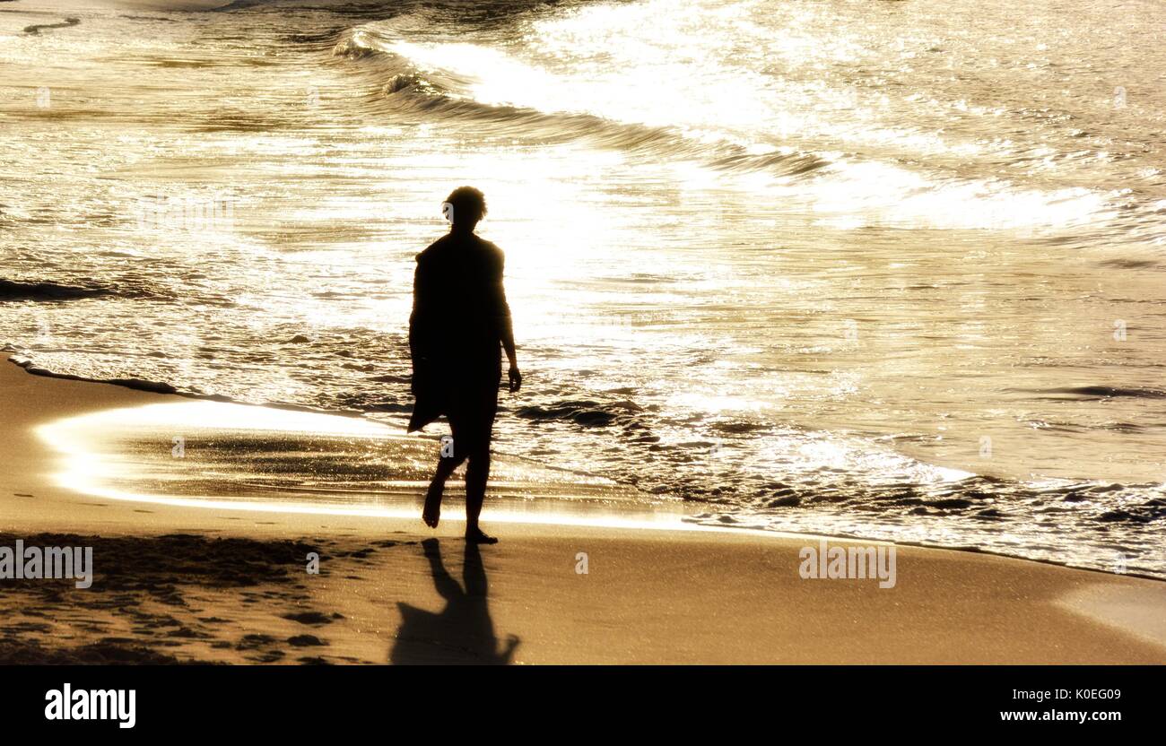 Woman in silhouette walking along a beach at sunset hi-res stock ...