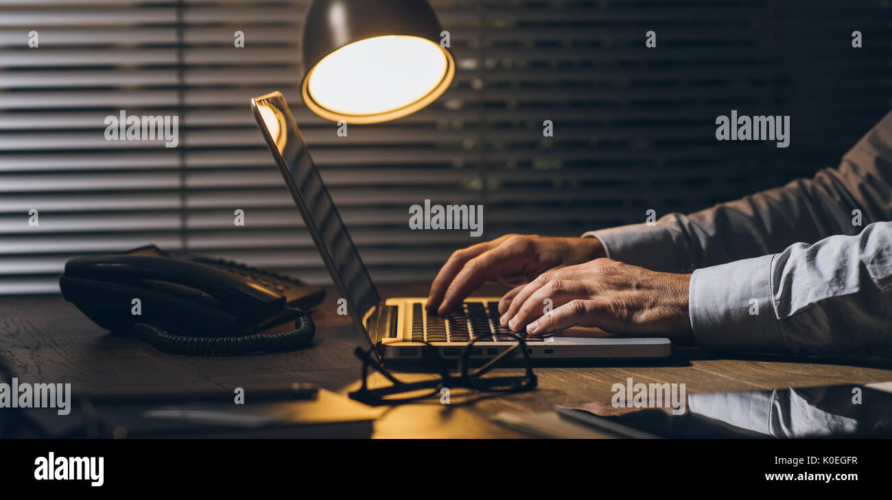 Corporate businessman working at office desk with his laptop late at ...
