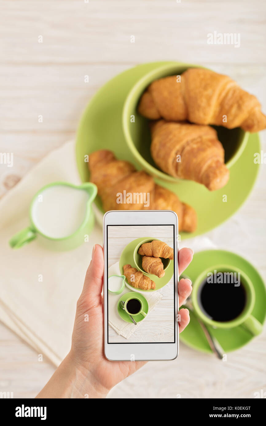 Female hand holding smart phone with picture of coffee with croissants ...