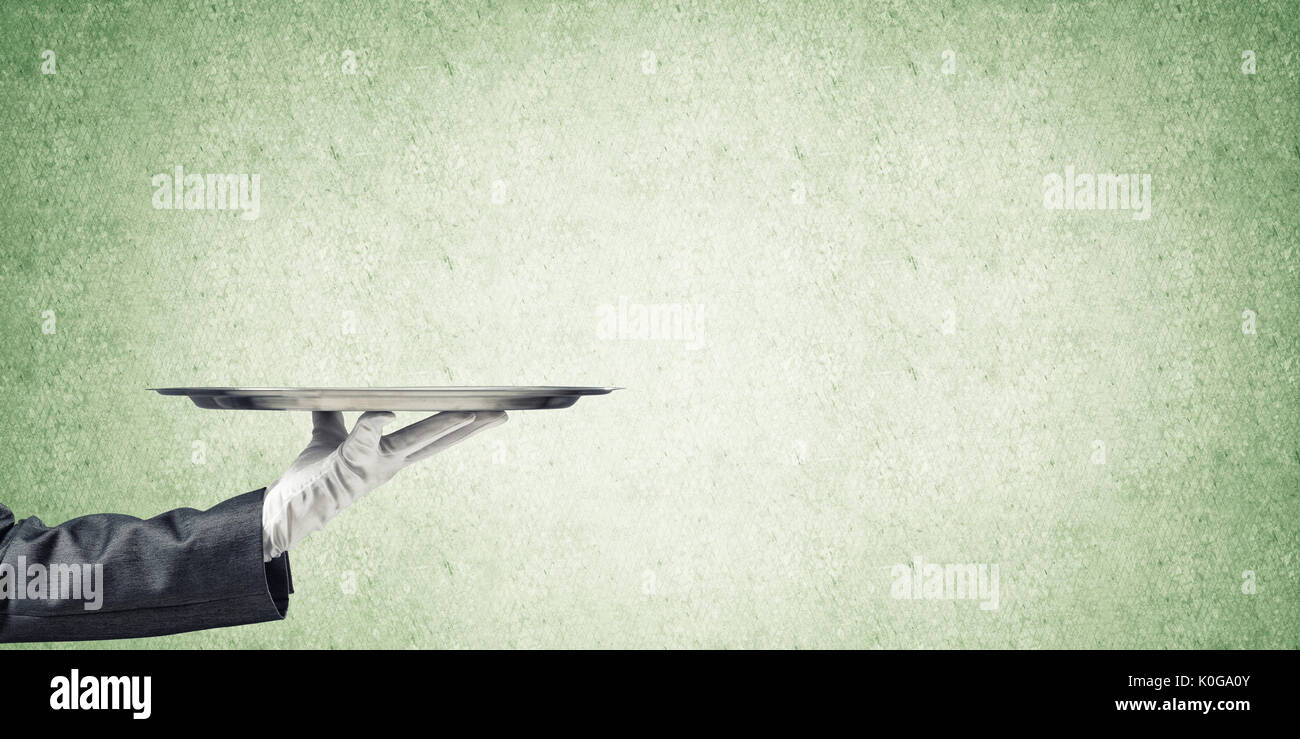 Hand of butler holding empty metal tray against green background Stock ...
