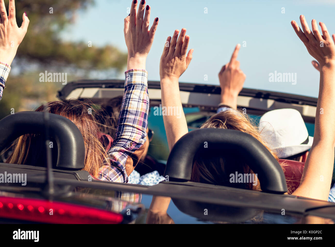Group of happy young friends in cabriolet with raised hands driving on ...