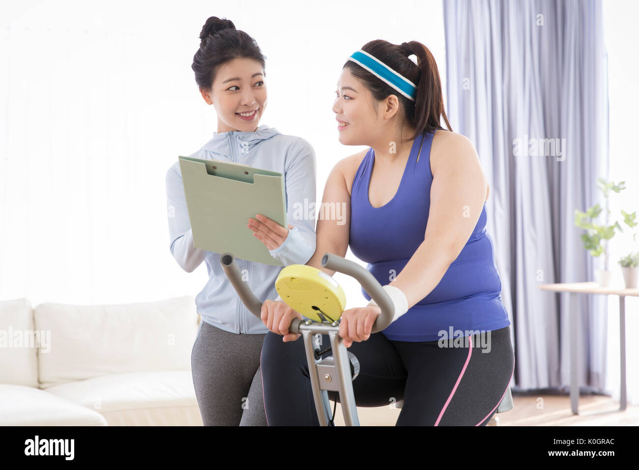 Young smiling slim female trainer and young smiling fat female trainee ...