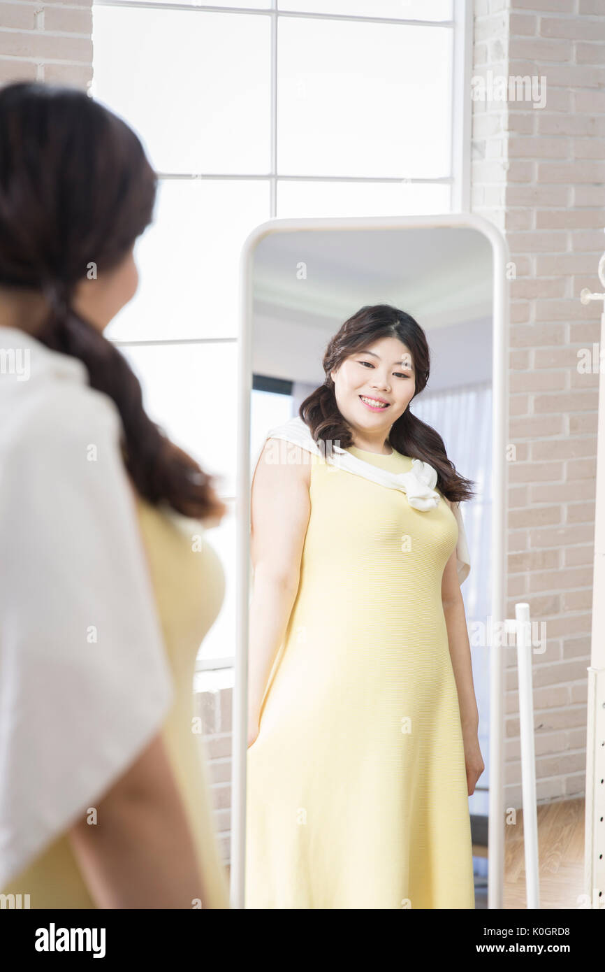 Young smiling fat woman in yellow dress looking in mirror Stock Photo ...