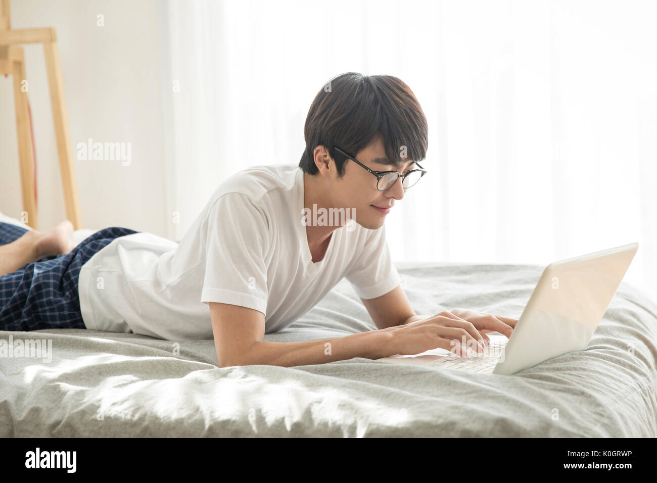 Single man using laptop lying face down on bed Stock Photo - Alamy