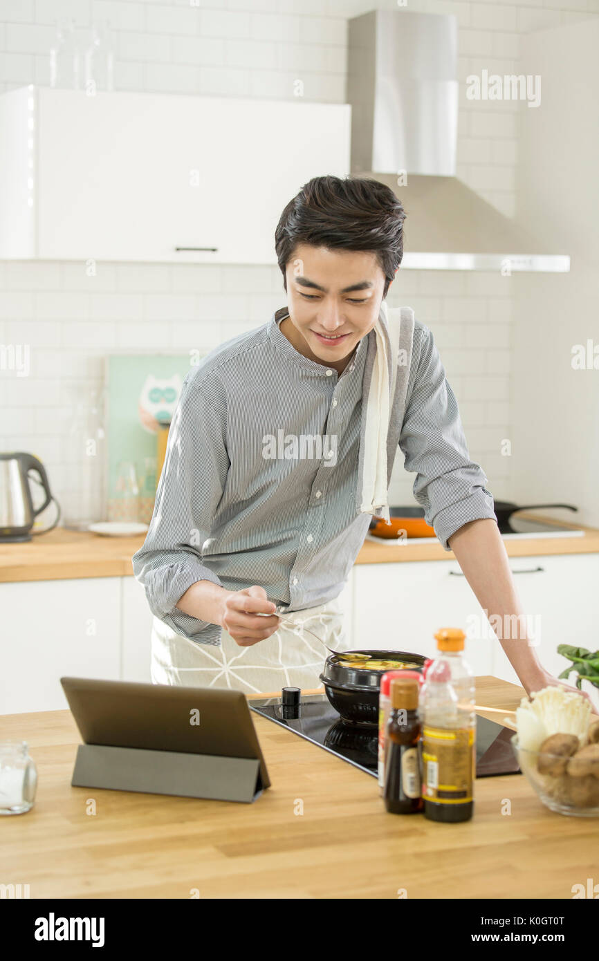 Smiling single man cooking with recipe on tablet Stock Photo - Alamy