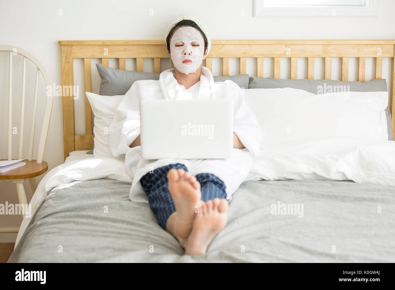 Grooming with beauty mask resting using notebook computer on bed Stock ...