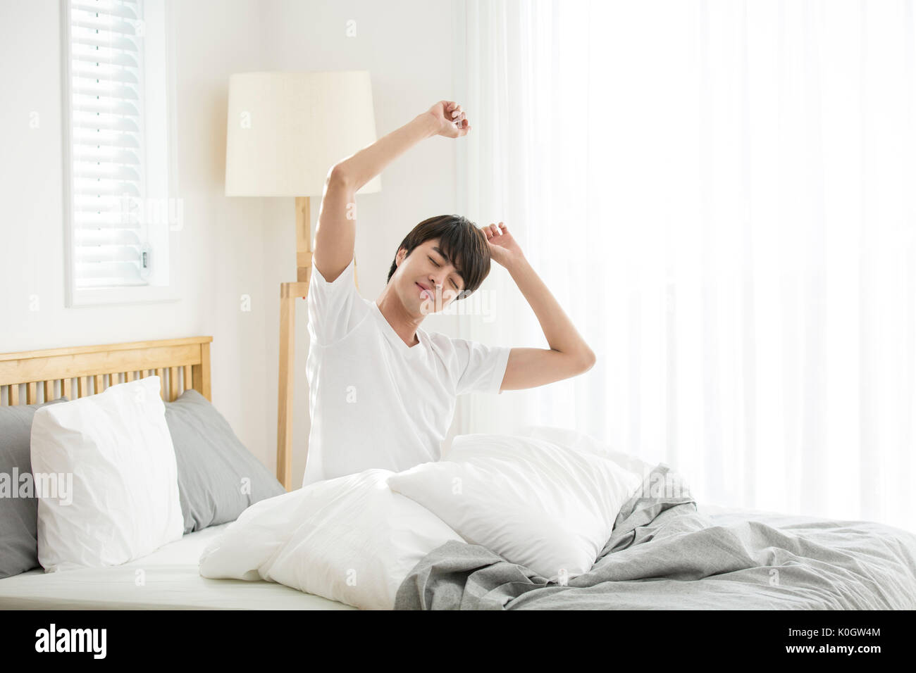 Single man stretching arms sitting on bed Stock Photo - Alamy