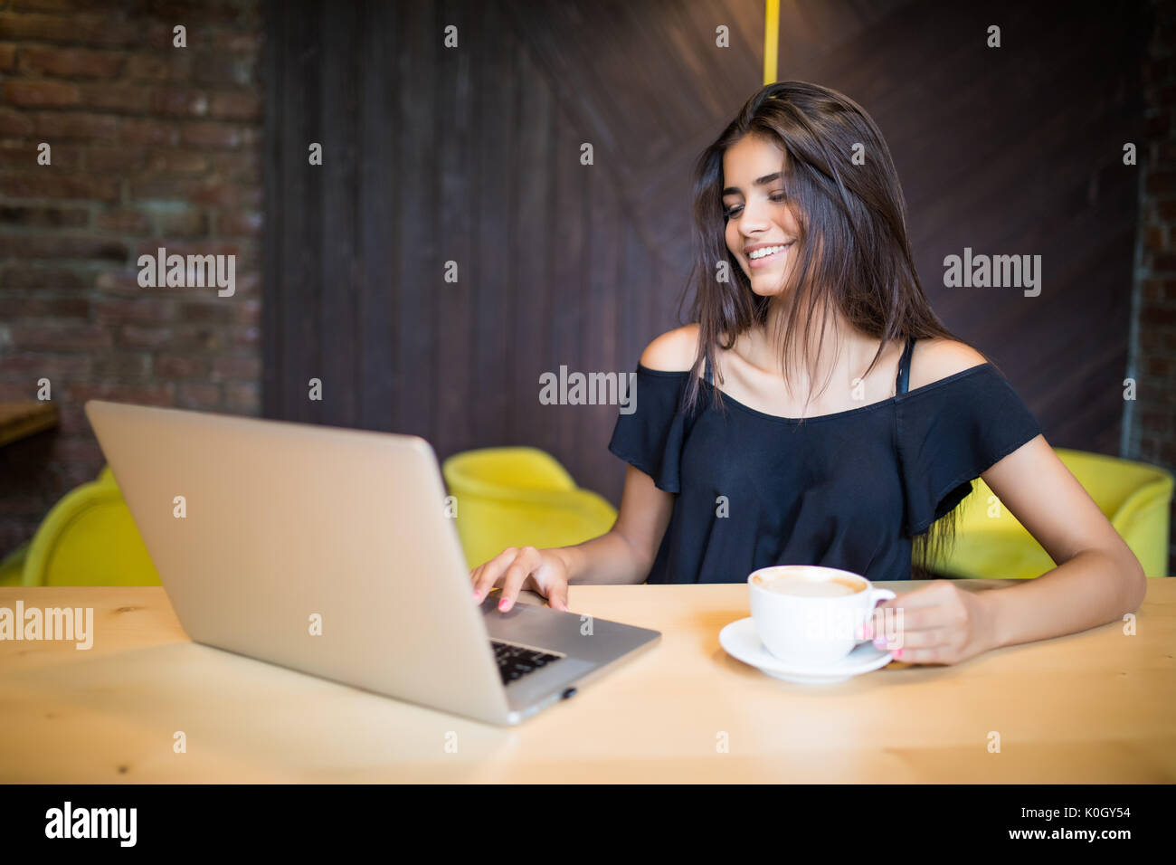 Young woman sitting in coffee shop at wooden table, drinking coffee and ...