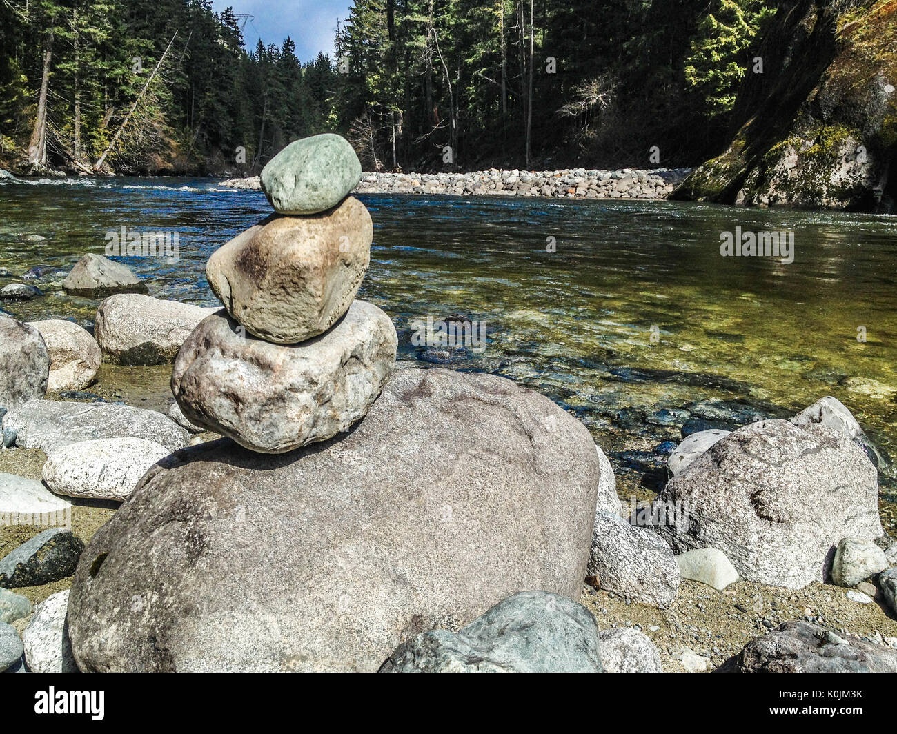 Piled rocks form a cairn next to a river with woods in the background ...