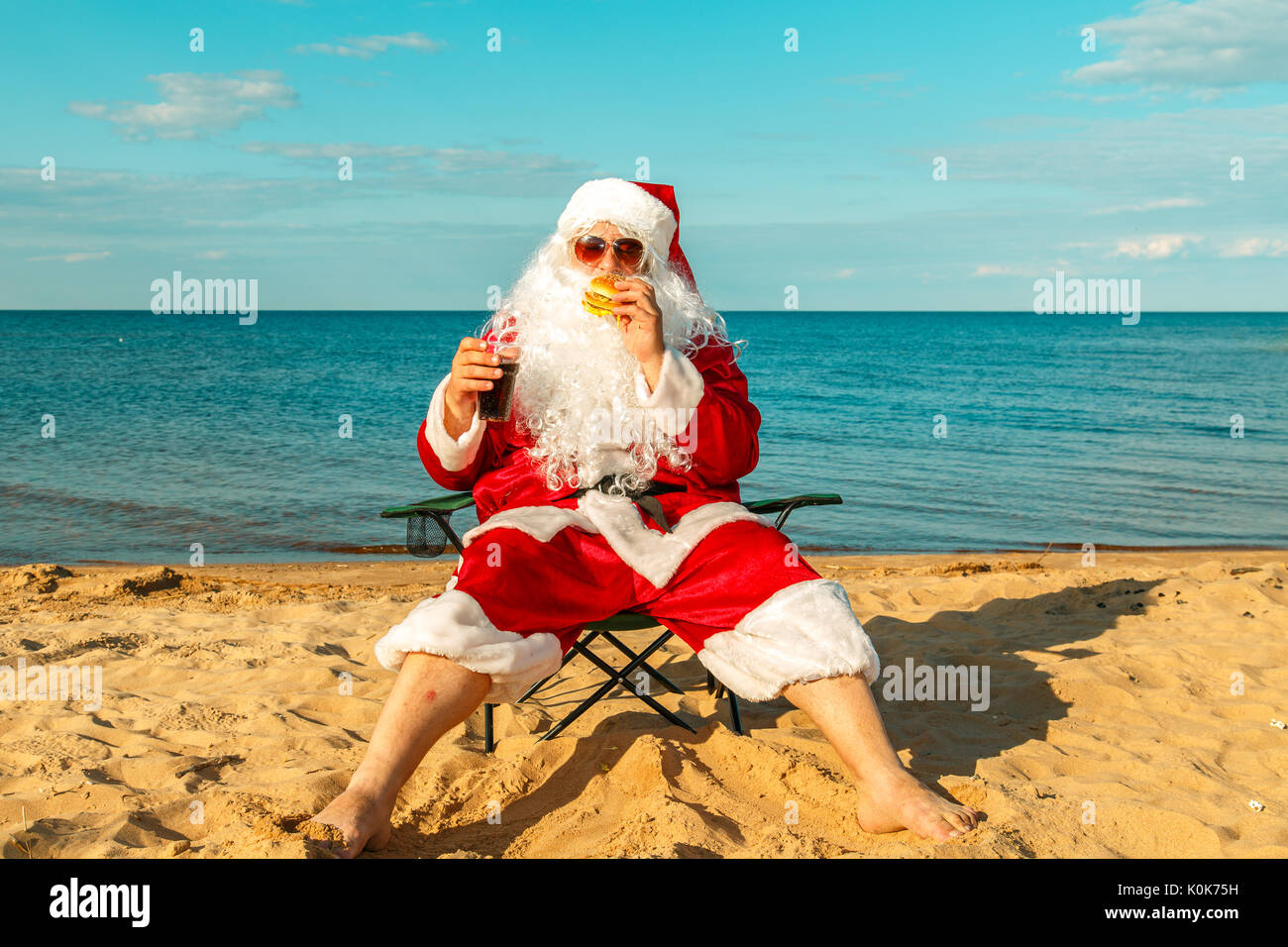 Santa Claus on the beach eating a hamburger. The concept of unhealthy ...