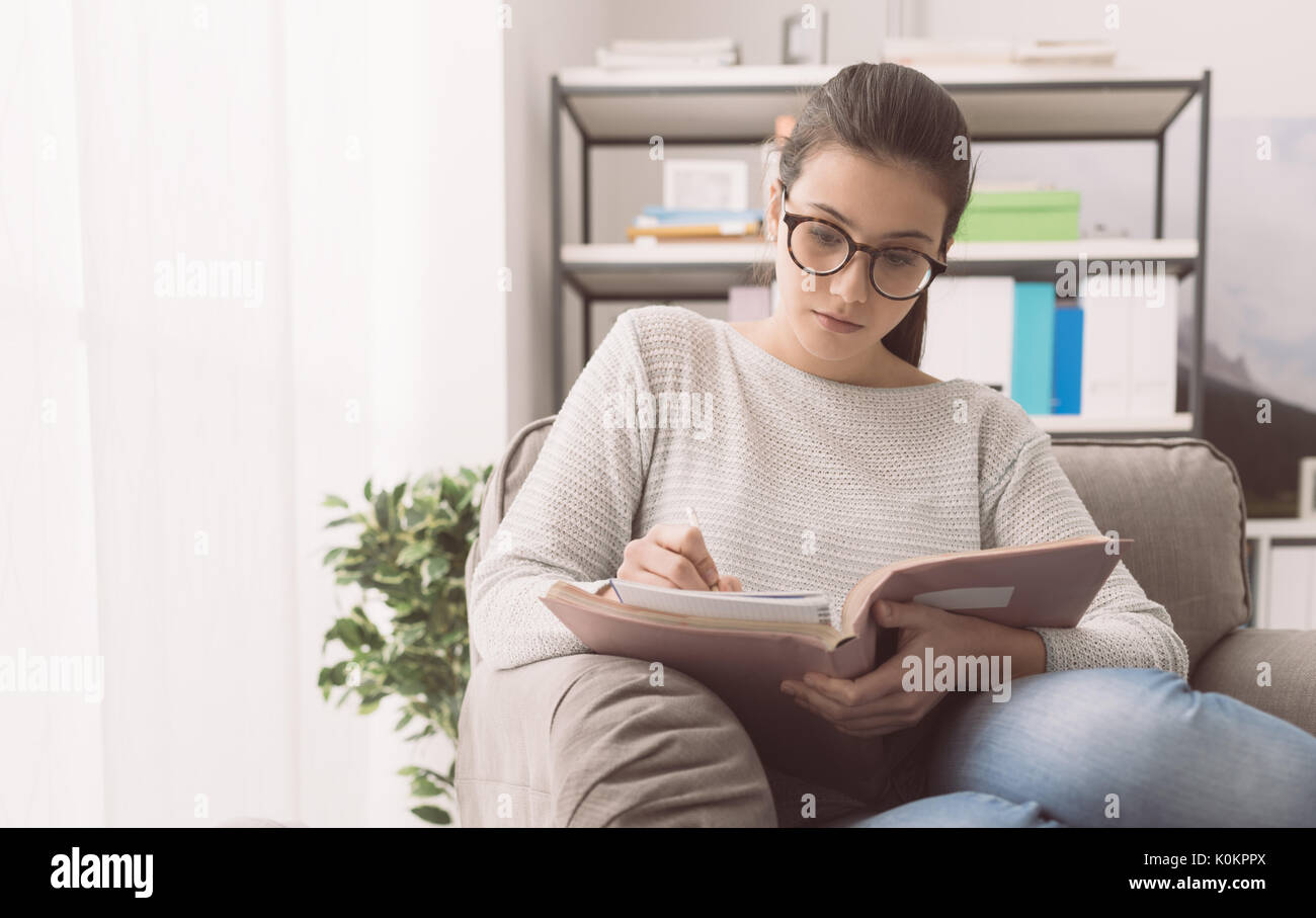 Smart female student doing homework, she is reading a book and holding ...