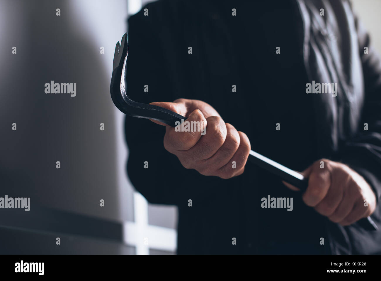 Dangerous burglar using a crowbar to break into a house late at night ...