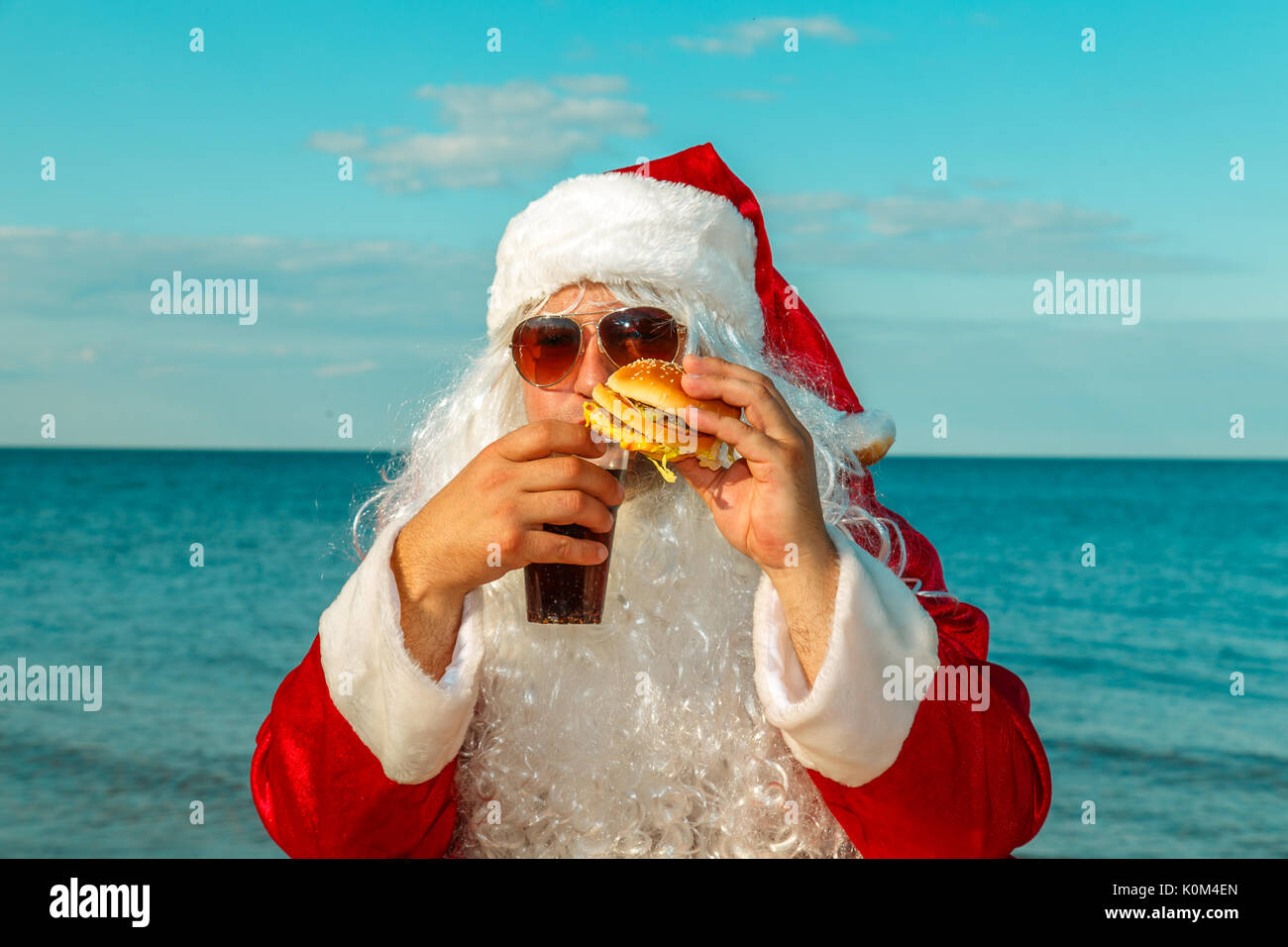Santa Claus on the beach eating a hamburger. The concept of unhealthy ...