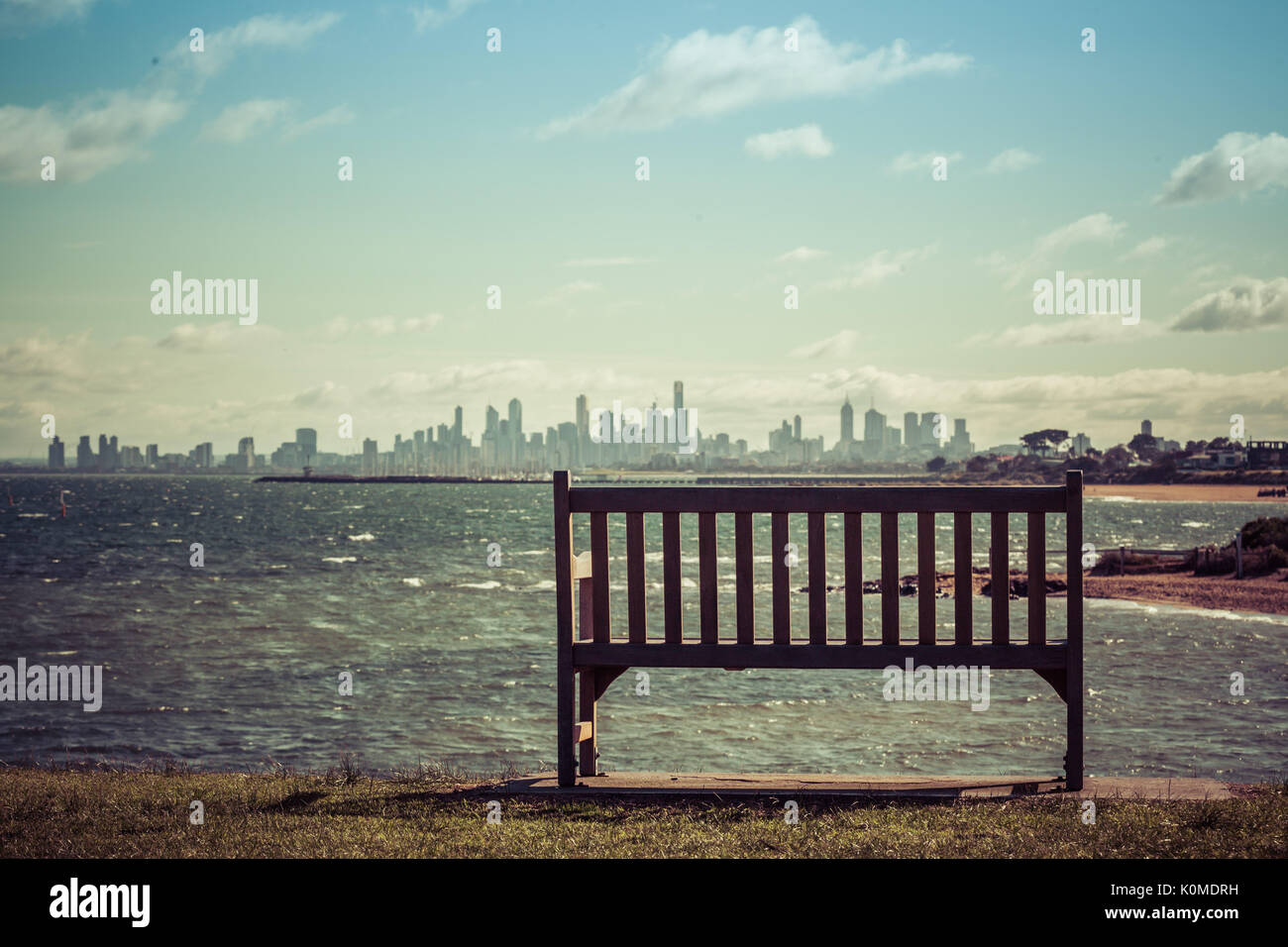 Empty wooden bench on ocean shore overlooking the skyline of Melbourne ...