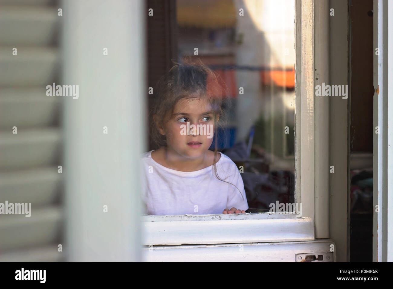 Cute little girl behind the window, being boring Stock Photo - Alamy