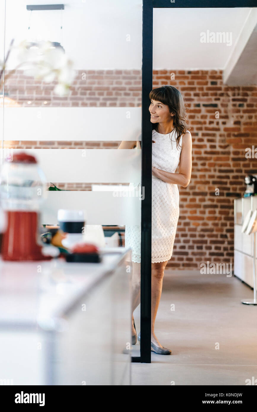 Businesswoman standing in office, looking around corner Stock Photo - Alamy