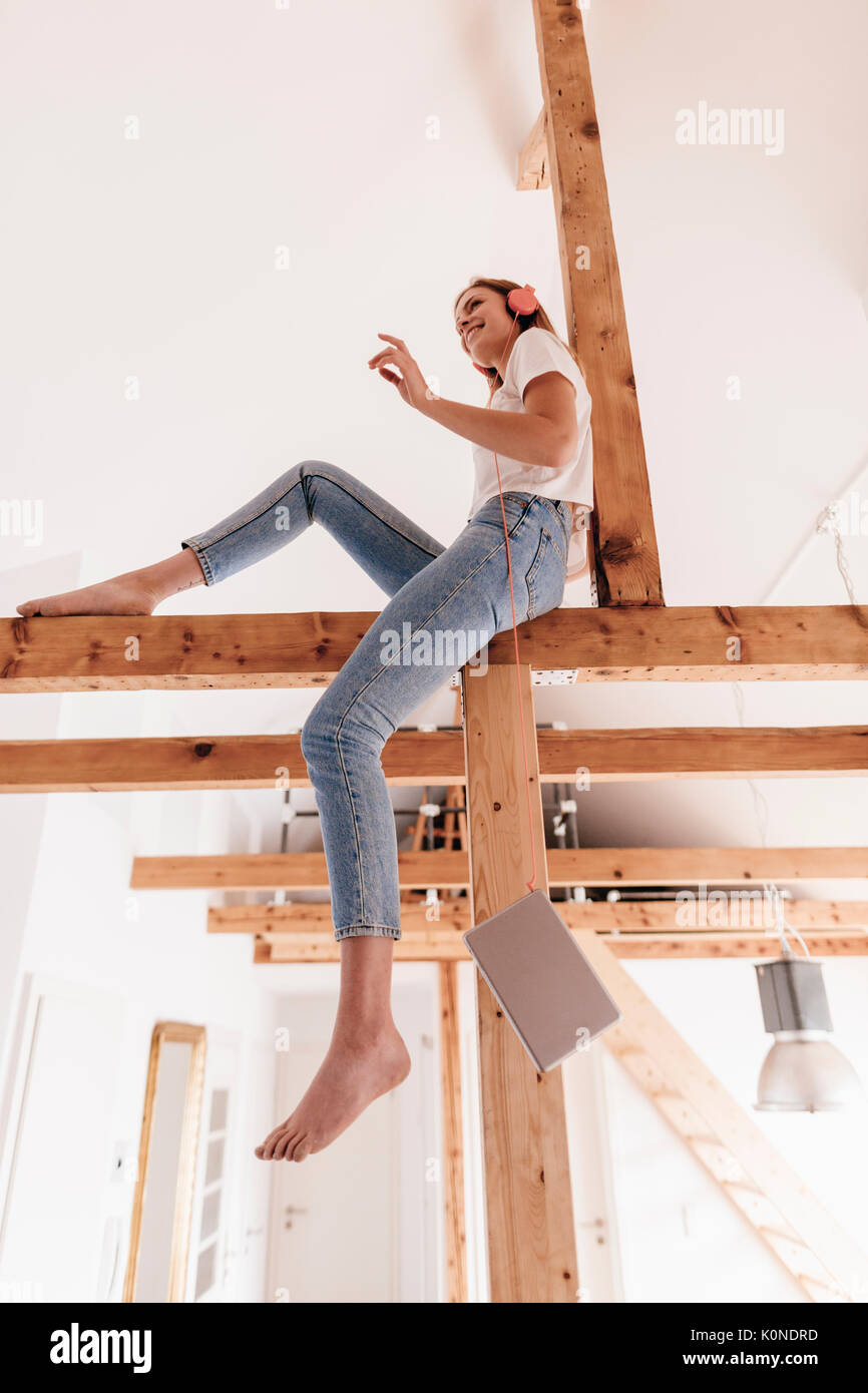 Carefree young woman sitting on ceiling joist, listening music Stock ...