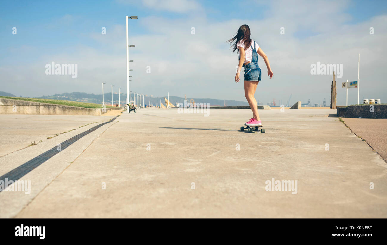 Back view of young woman longboarding on beach promenade Stock Photo ...