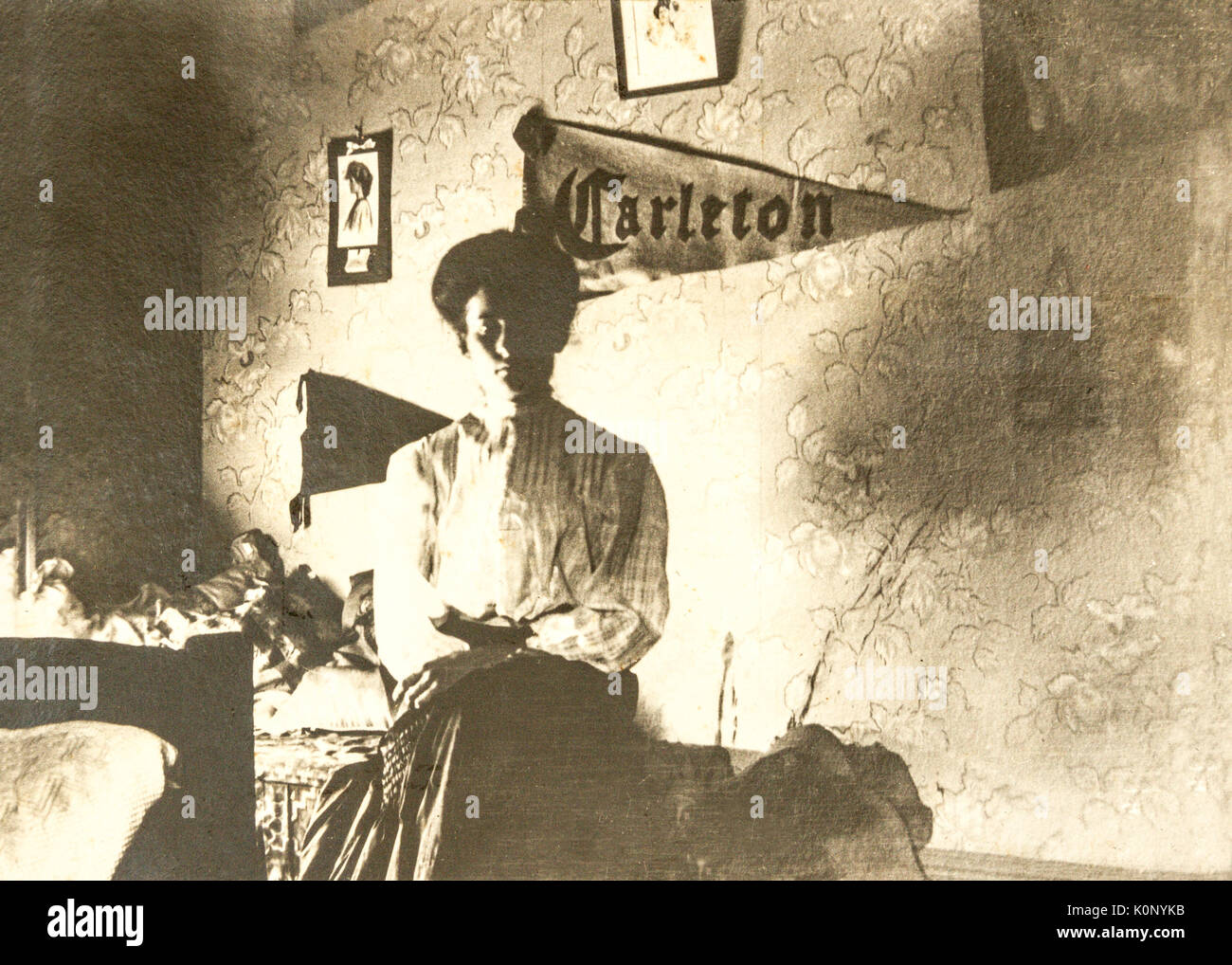 A young woman sitting in a bedroom with a pennant for Carleton College ...