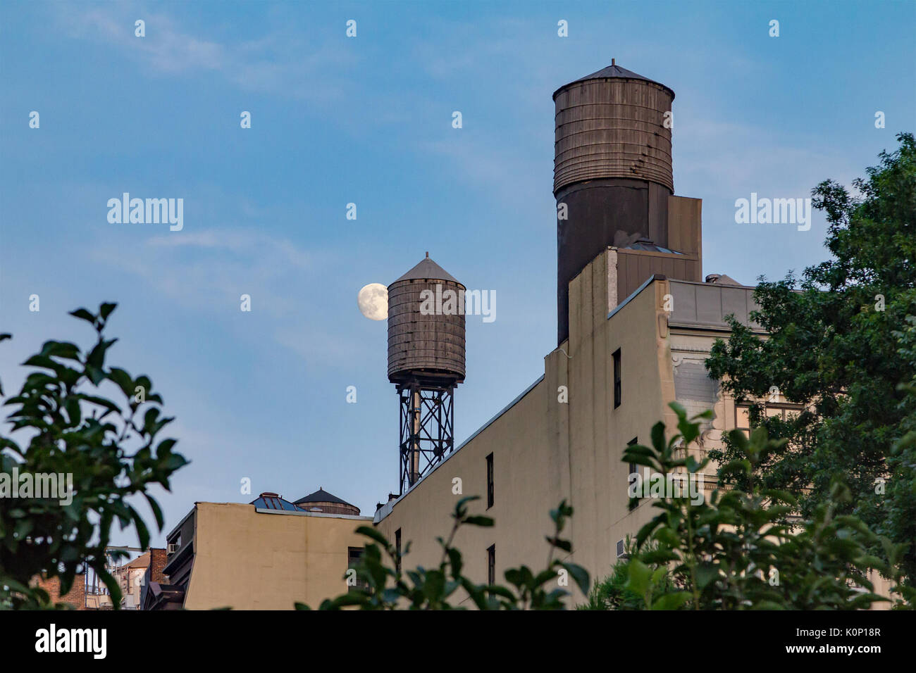 Full moon rising behind water tower on the roof of buildings in New ...