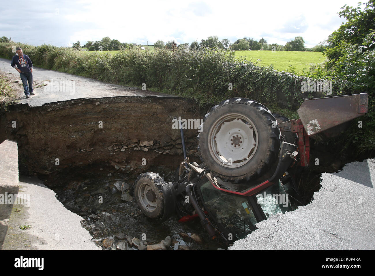 A man looks at a tractor which has fallen into a river after a road ...