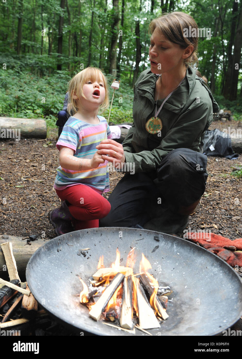Woman and young girl toast a marshmallow over a fire pit in a forest ...