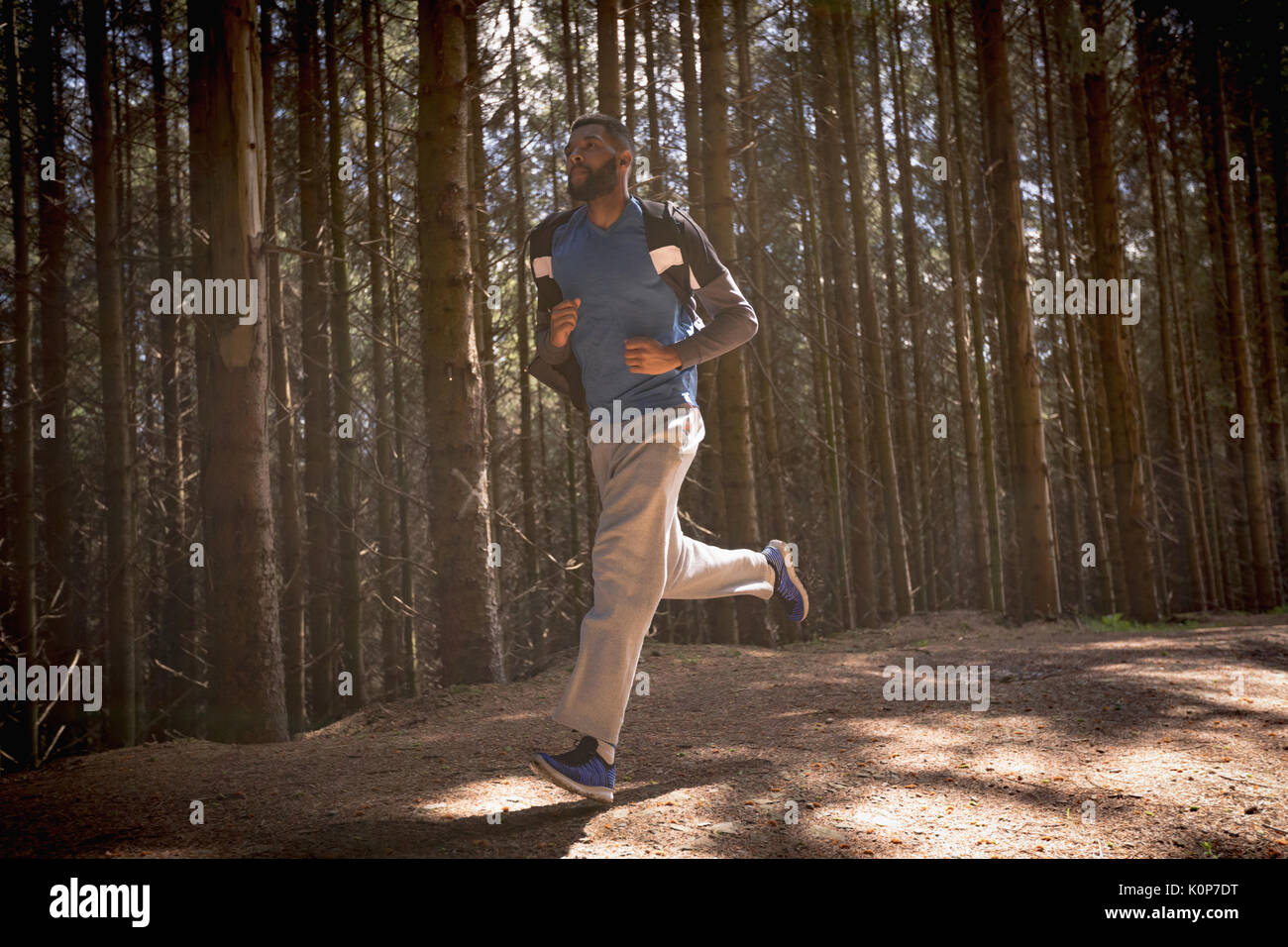 Young man running on road by trees in forest Stock Photo - Alamy